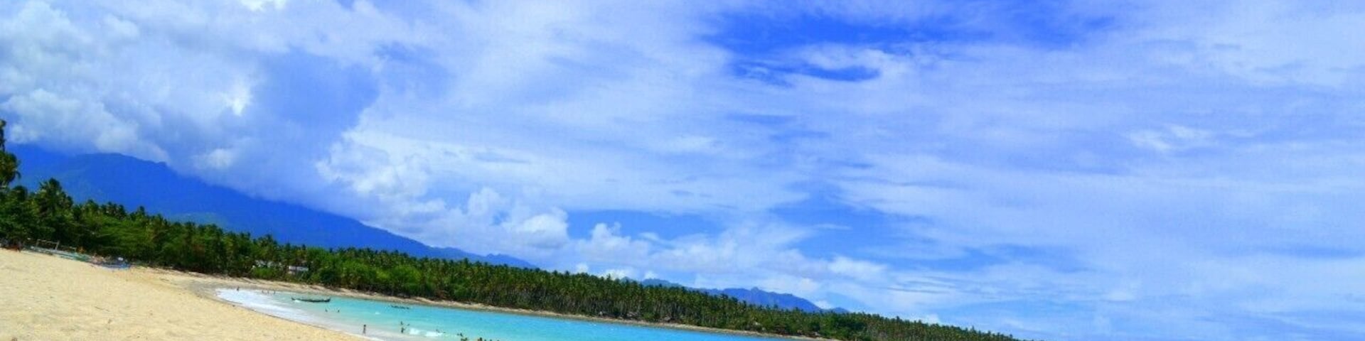 Uma praia com águas turquesa cristalinas, areal arenoso e uma colina arborizada ao fundo.