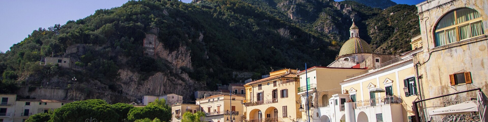 Uma vila costeira com edifícios, uma praia e montanhas ao fundo.