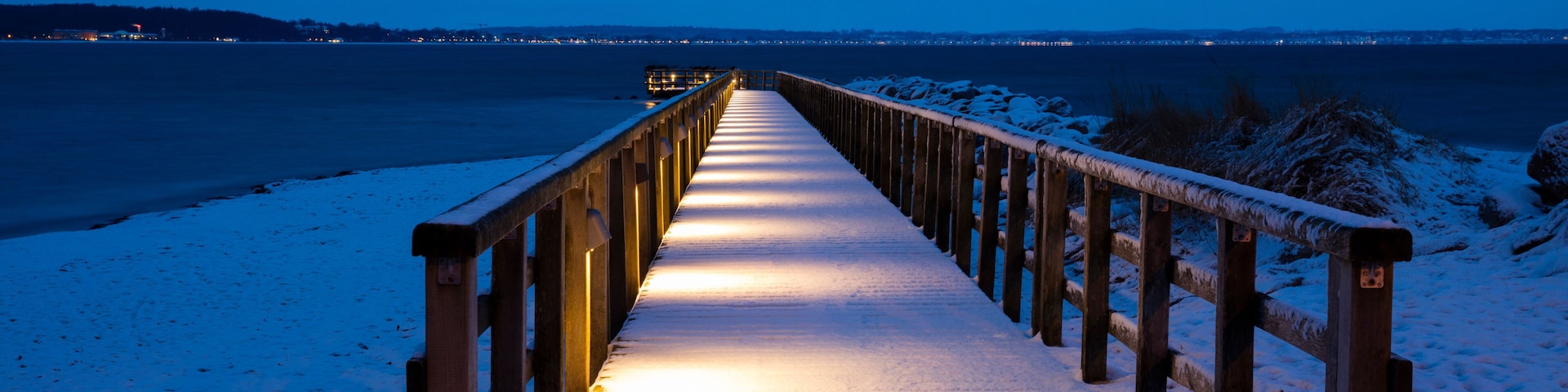 Um cais de madeira coberto de neve que se estende sobre a água ao entardecer.