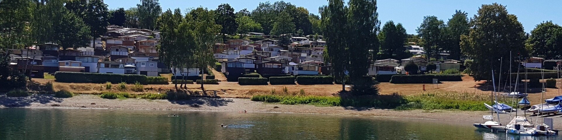 Um parque de campismo à beira do lago, com caravanas e barcos.