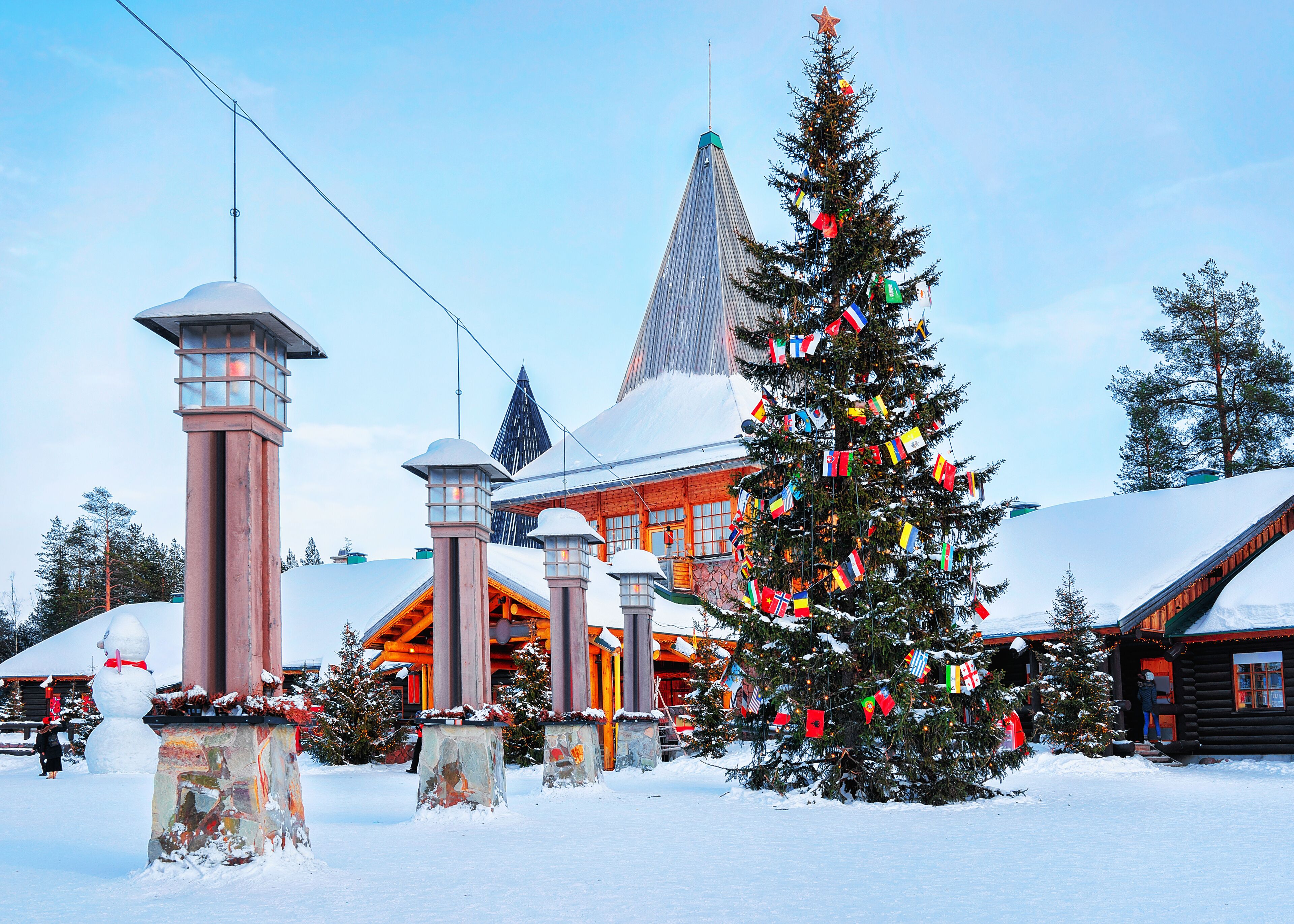 Paisagem coberta de neve com um pinheiro decorado para o Natal, um boneco de neve e uma cabana de madeira.