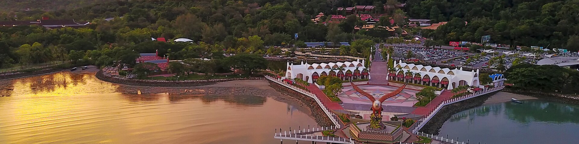 Um parque à beira do lago com um coreto branco, uma ponte e vegetação exuberante ao redor.