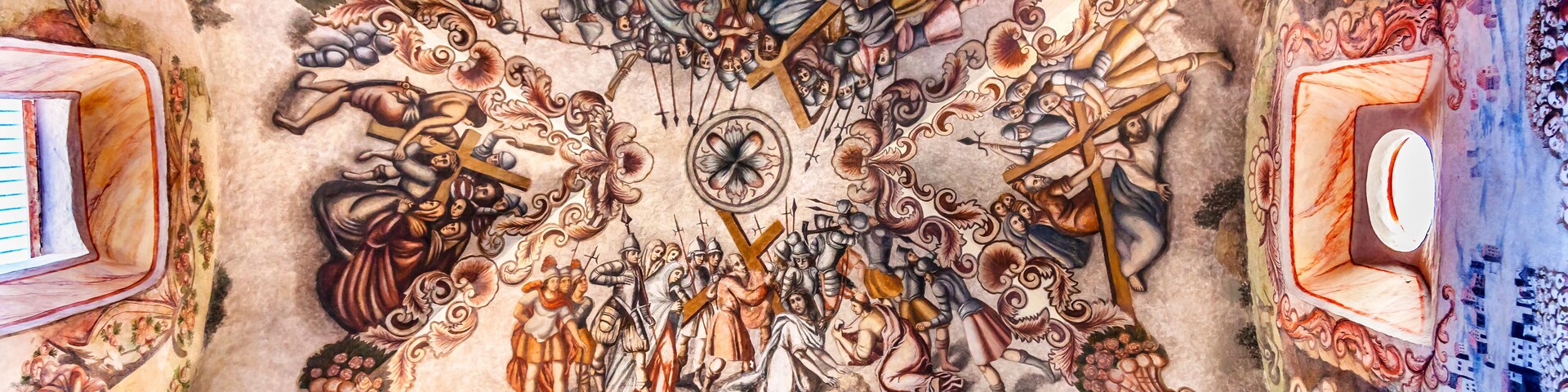 Um afresco detalhado no teto, com cenas e figuras religiosas, cercado por elementos arquitetônicos ornamentados.