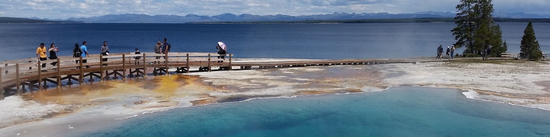 Um lago azul e límpido com um cais de madeira e pessoas caminhando.