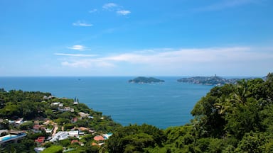 Paisagem costeira com vegetação densa, céu azul límpido e vista para o mar com ilhas ao longe.