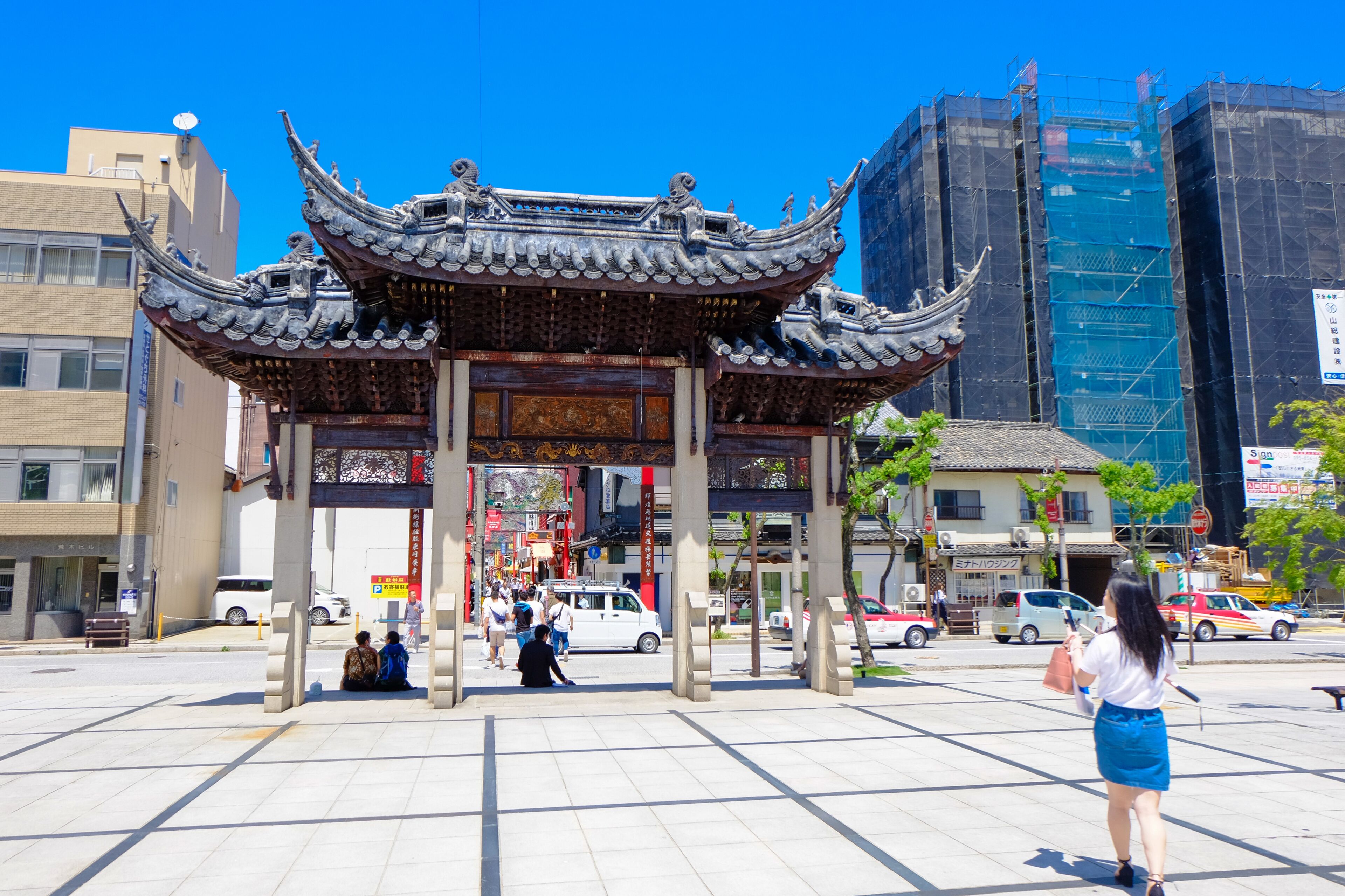 Um portão tradicional chinês com design ornamentado no telhado, um edifício moderno com andaimes e um céu azul límpido.