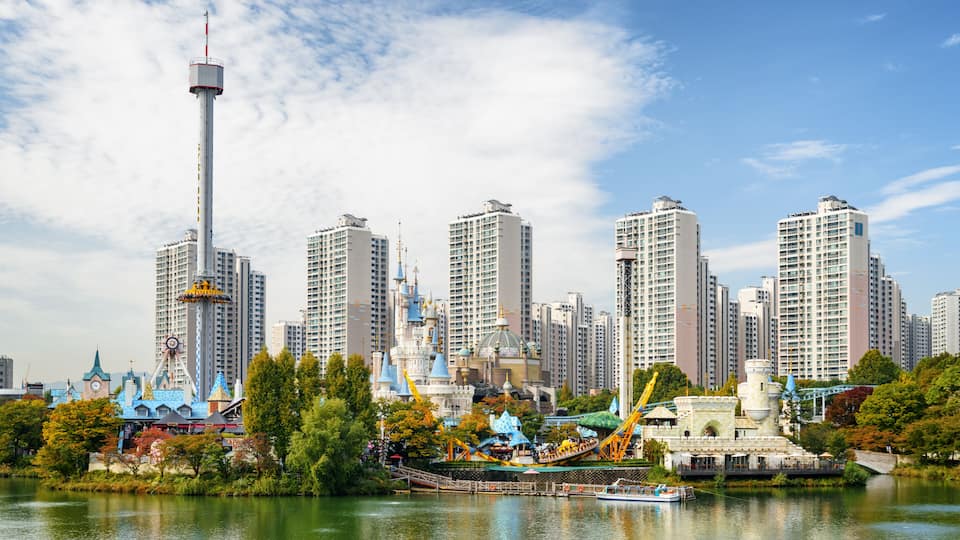 Paisagem urbana com uma torre imponente, um corpo d'água e um parque com estruturas coloridas.