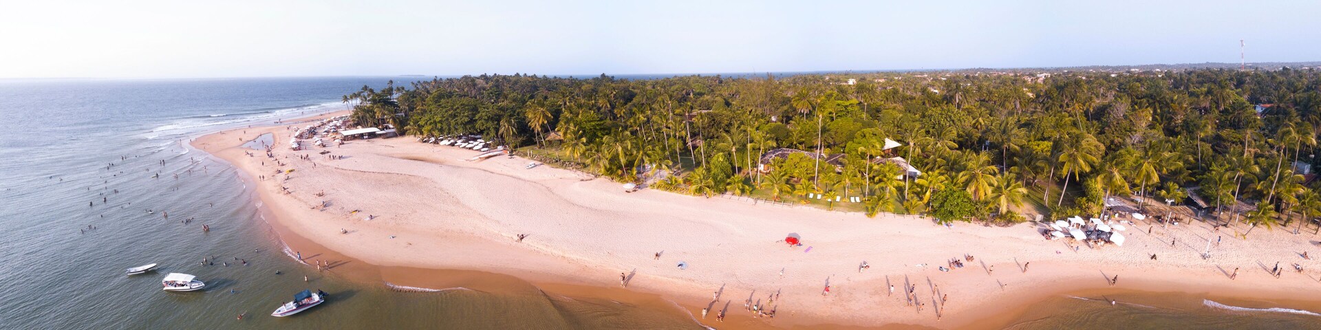 Uma praia com barcos, palmeiras e céu claro.