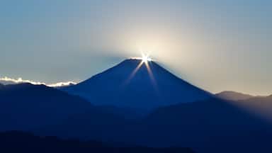 Uma montanha com um sol brilhante aparecendo atrás dela.