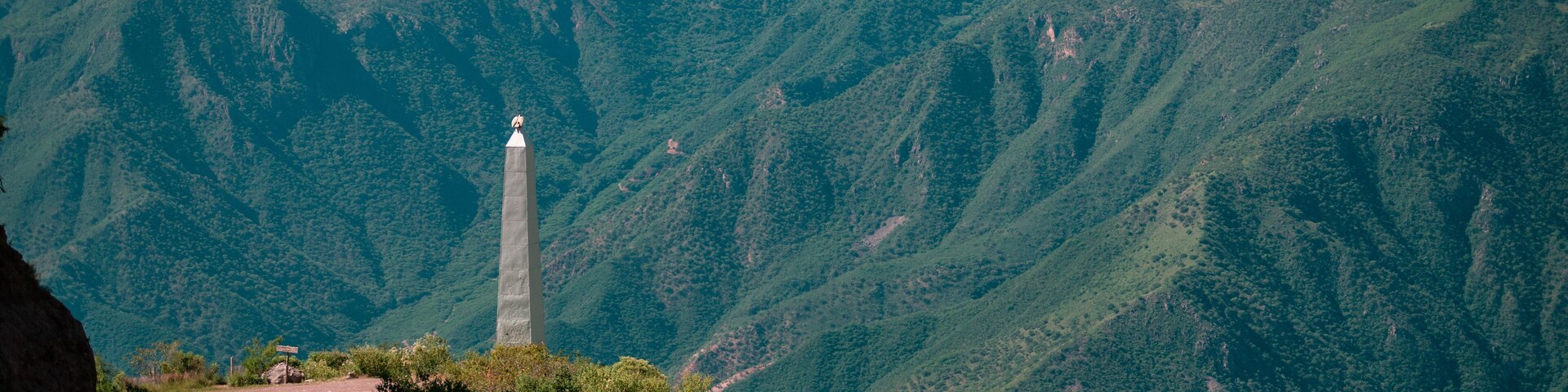 Um monumento imponente em área montanhosa, com densas florestas verdes.