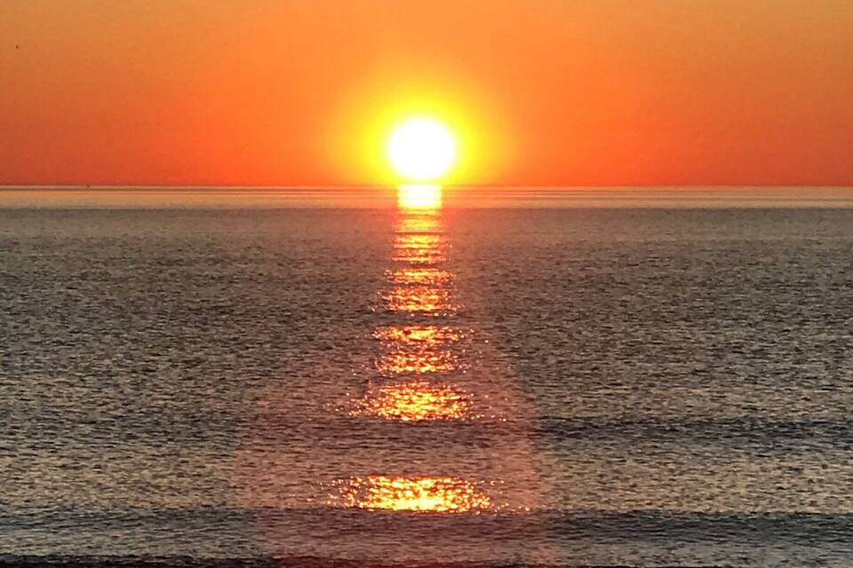 Um pôr do sol sobre uma praia com o sol se refletindo na água.