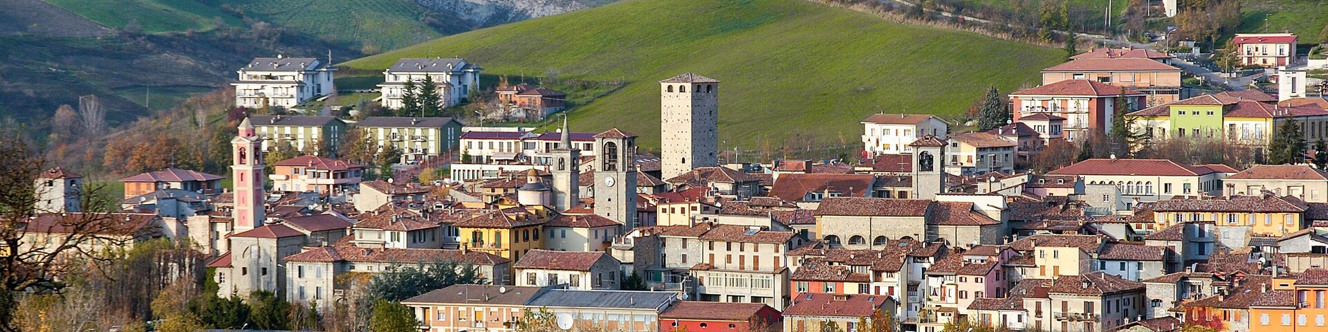 Uma cidade aninhada em um vale, com uma torre de igreja imponente, cercada por colinas ondulantes e campos verdes.
