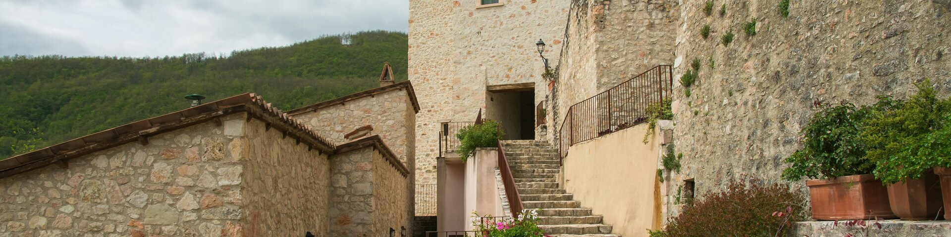 Uma escadaria de pedra leva a um edifício com telhado verde, cercado por vegetação e plantas em vasos.