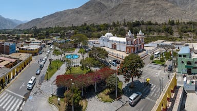 Uma cidade com uma praça central, uma igreja e montanhas ao fundo.