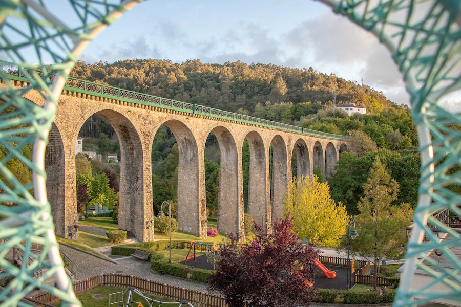 Um viaduto de pedra com várias arcos sobre um parque com equipamentos de recreio.