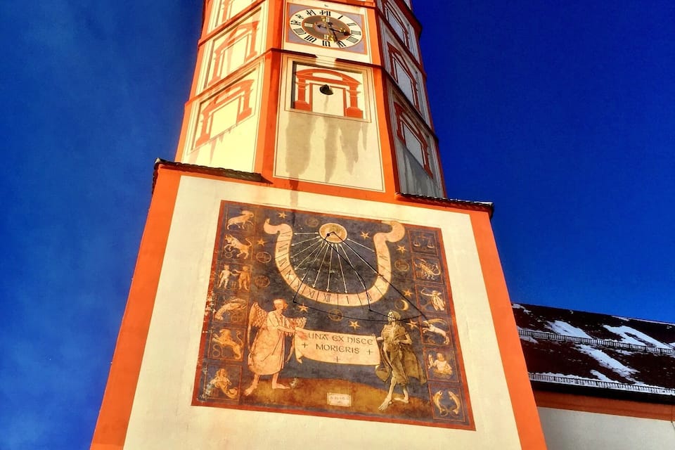 Uma torre com um relógio e um mural de um signo do zodíaco.