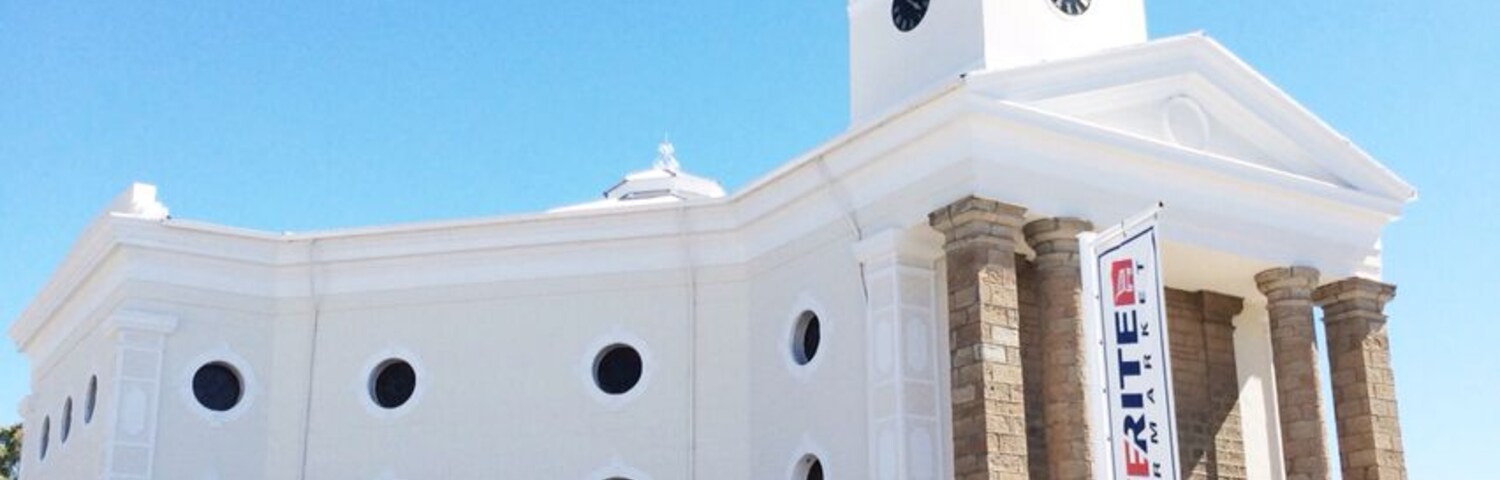 Uma igreja branca com uma torre de relógio e uma placa com a inscrição 'SAVERITE'.
