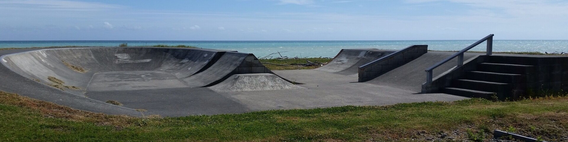 Um parque de skate com várias rampas e uma escadaria que dá para uma praia.