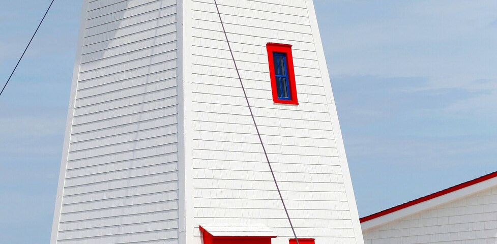 Um farol branco com detalhes vermelhos e uma porta vermelha, rodeado por caixas azuis e brancas.