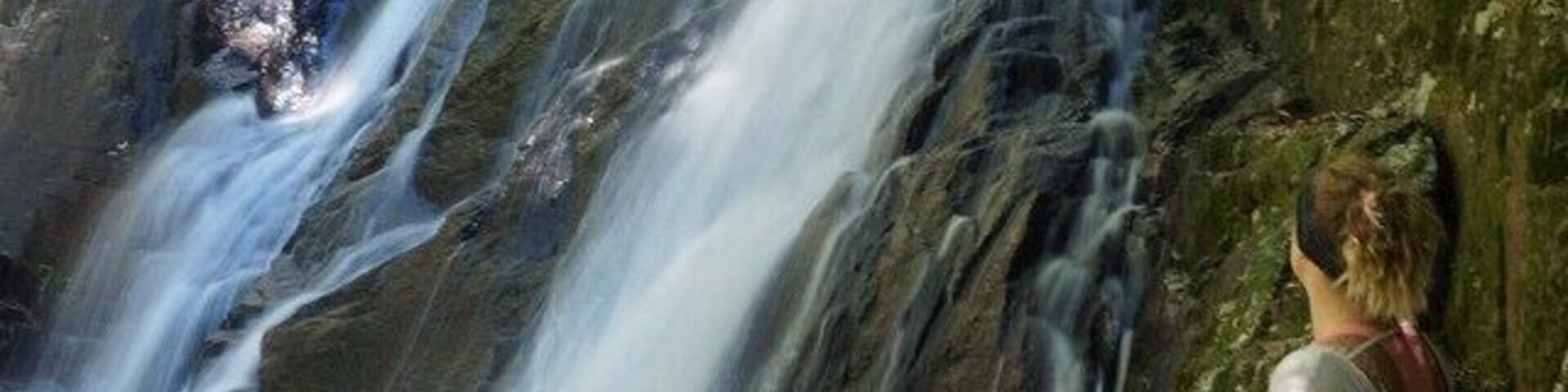 Uma cascata desce uma falésia rochosa, com uma pessoa sentada sobre a rocha.