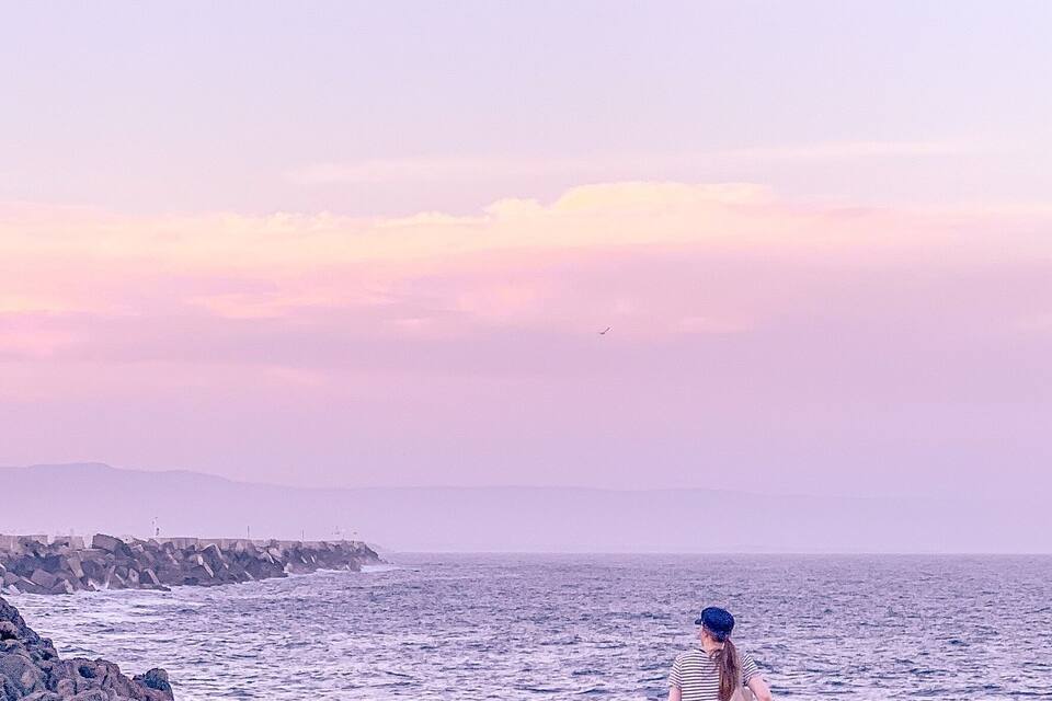 Uma pessoa em terreno rochoso à beira-mar durante o pôr do sol.