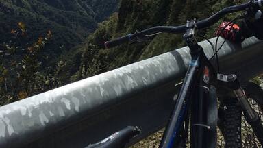 Uma bicicleta de montanha encostada em uma grade de proteção com vista para um vale com vegetação exuberante e montanhas ao longe.