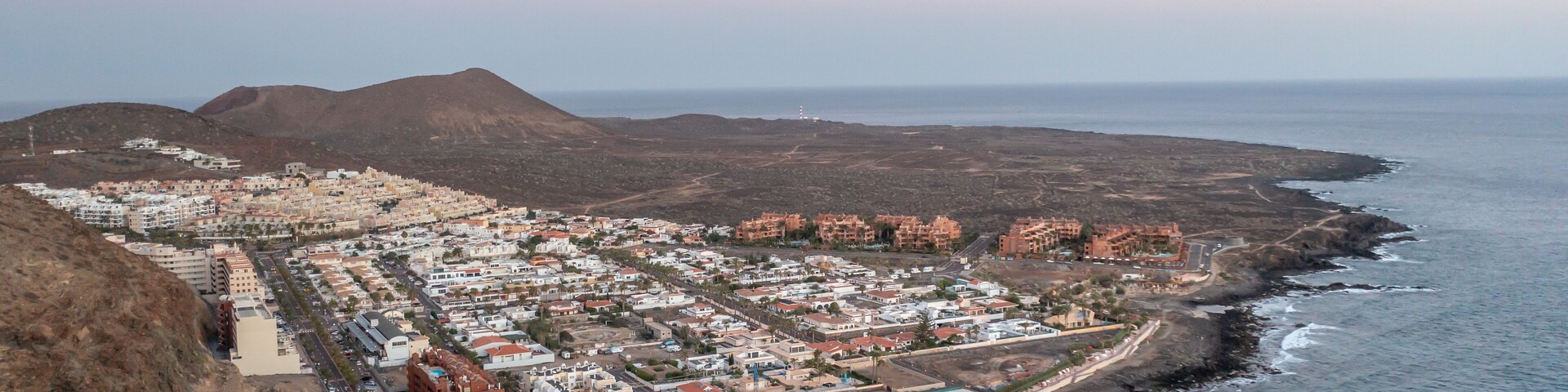 Vista aérea de uma vila costeira com edifícios, uma praia e um farol.