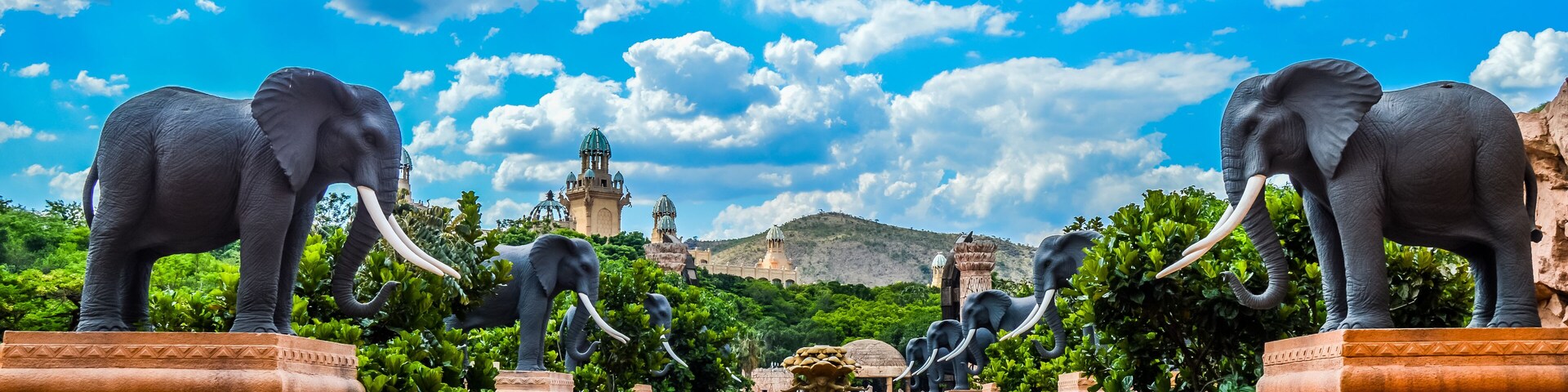 Uma passagem ladeada por estátuas de elefantes que leva a um edifício histórico com cúpulas.