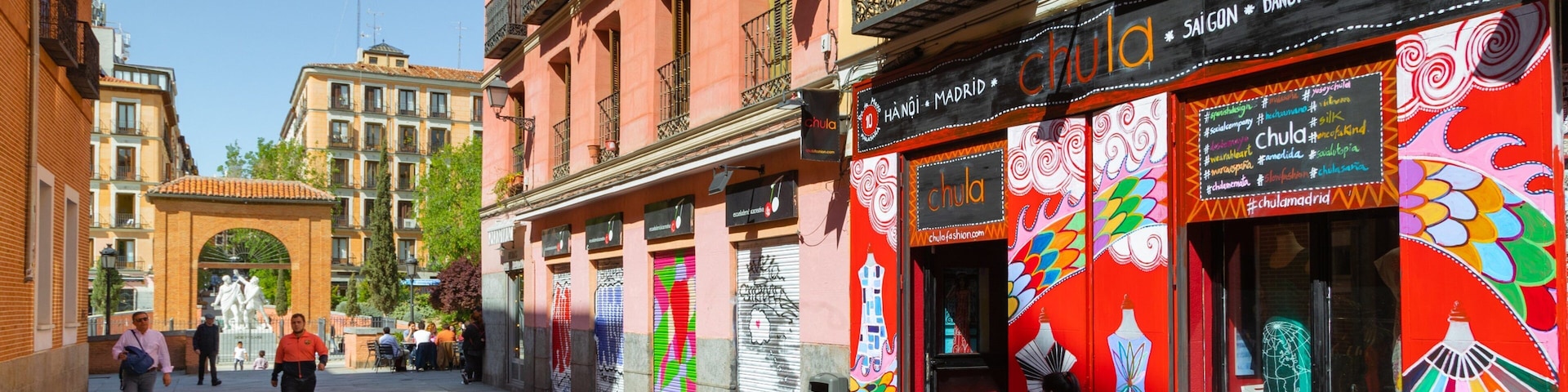 Uma rua com fachadas coloridas, incluindo uma com um mural de uma mulher e um vestido.