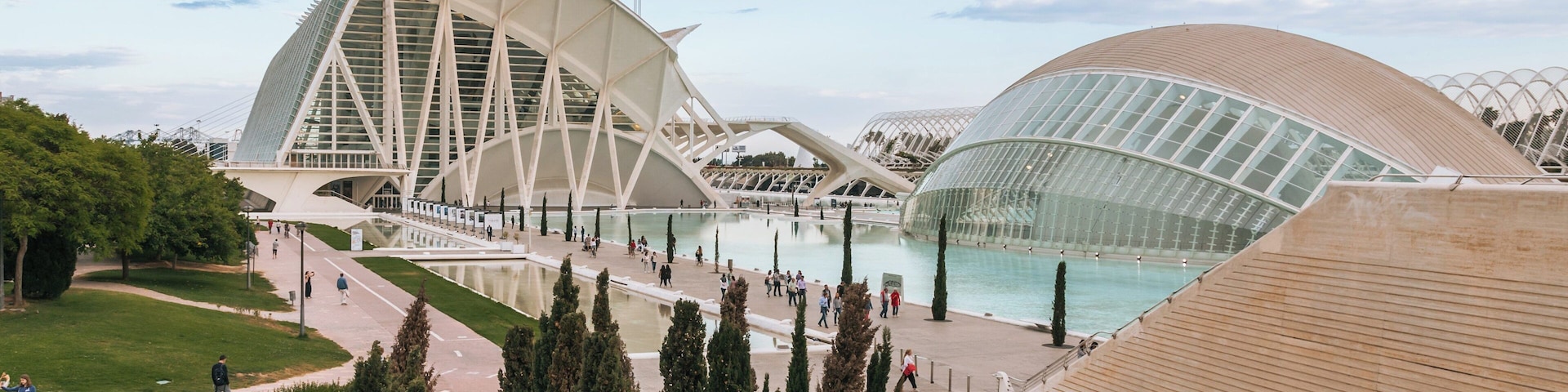 Um complexo arquitetônico moderno com um edifício central imponente, uma piscina refletora e vegetação ao redor.