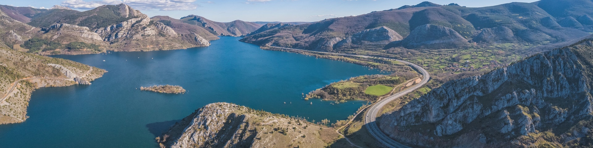 Paisagem montanhosa com uma estrada sinuosa, uma grande extensão de água e uma pequena ilha.