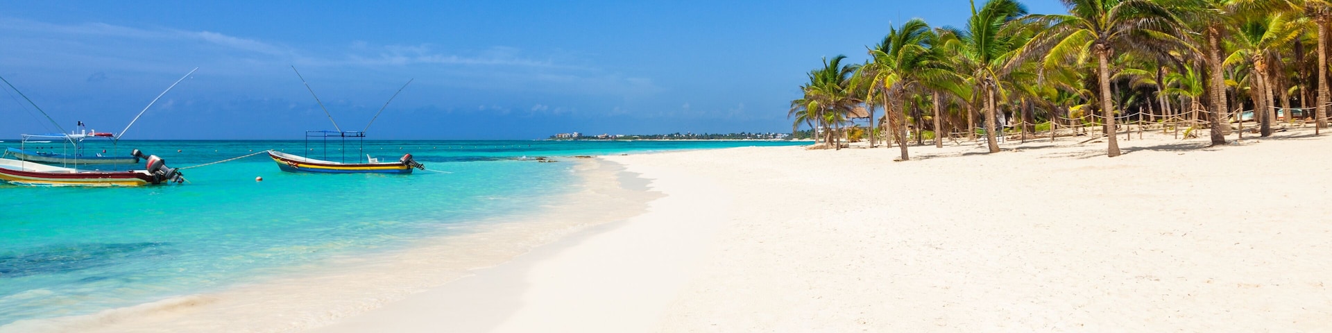 Uma praia com areia branca, águas azul-turquesa e palmeiras.