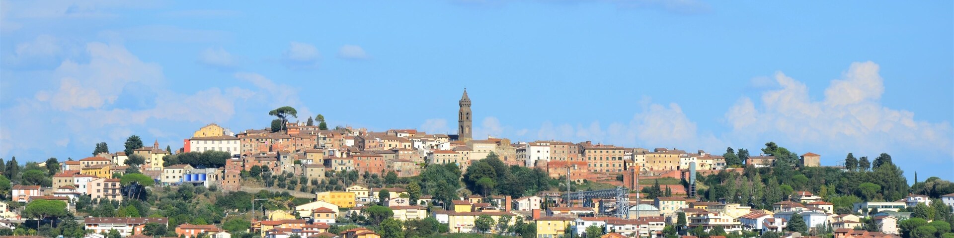 Vista panorâmica de uma cidade histórica, com uma torre de igreja imponente e uma fortaleza no alto de uma colina.
