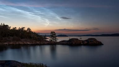 Um lago calmo ao pôr do sol, com margens rochosas e árvores.