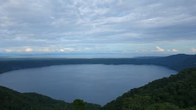 Um lago extenso rodeado por colinas arborizadas sob um céu parcialmente nublado.