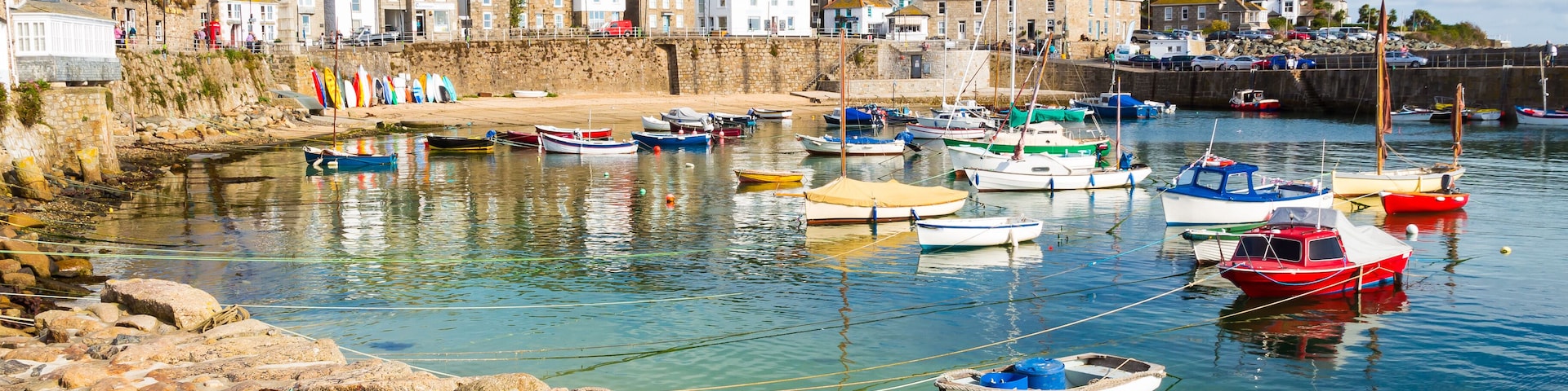Um porto com muitos barcos pequenos, uma parede de pedra e casas ao fundo.
