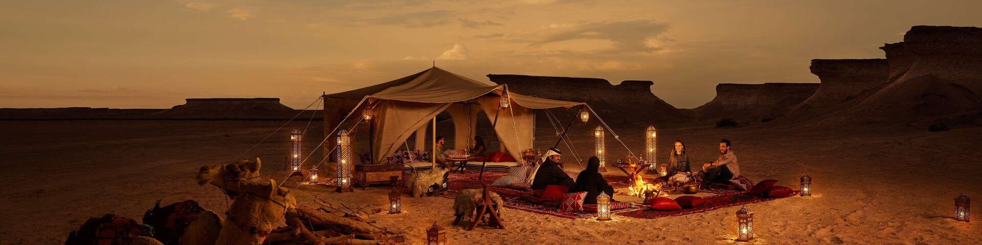 Acampamento no deserto com tendas, pessoas e um camelo.