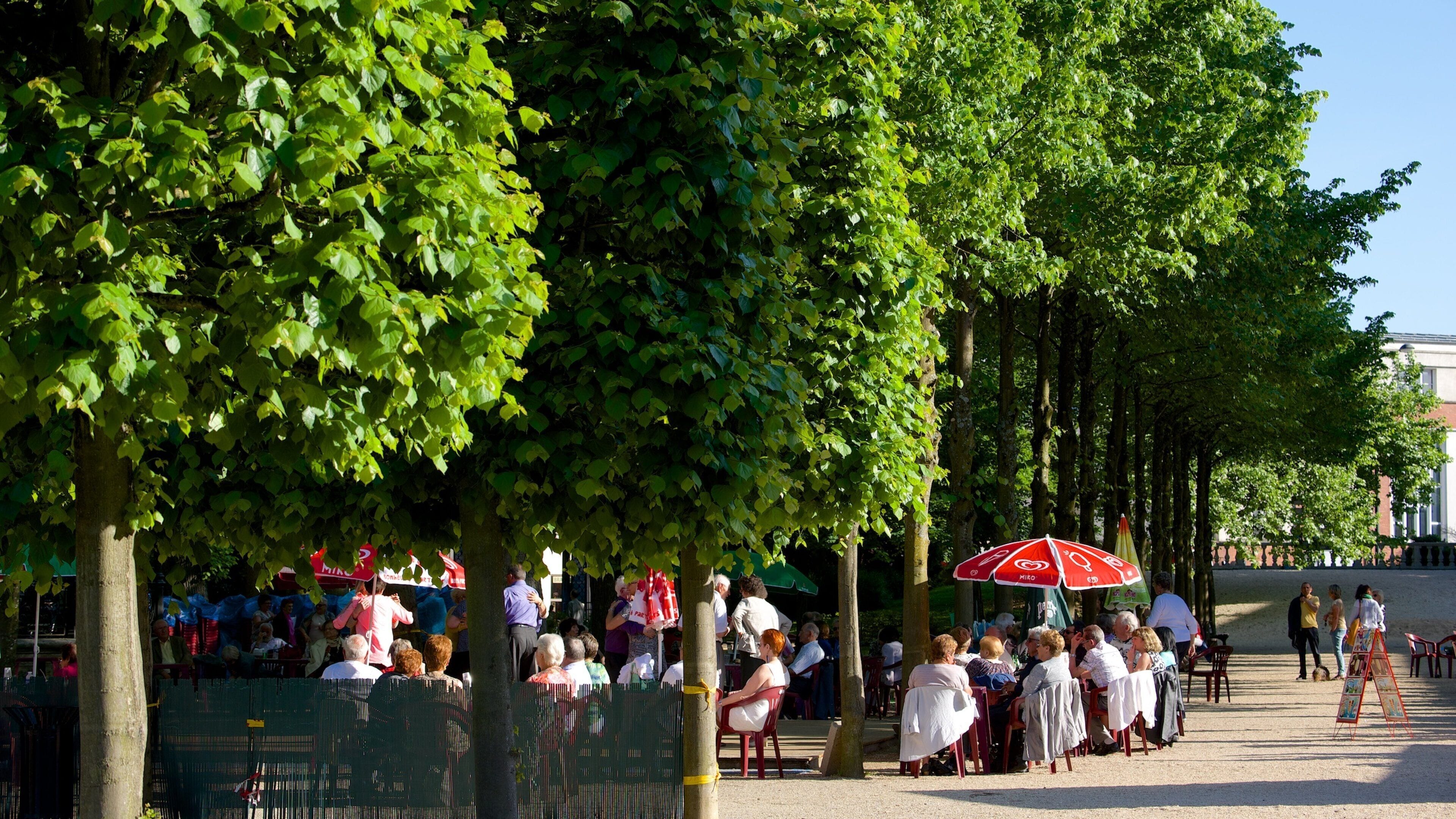 Um parque com pessoas sentadas sob árvores e guarda-sóis vermelhos.