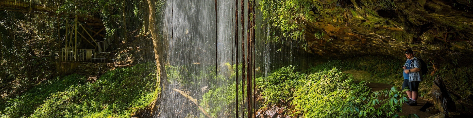 Uma cascata em uma área arborizada, com uma pessoa próxima.