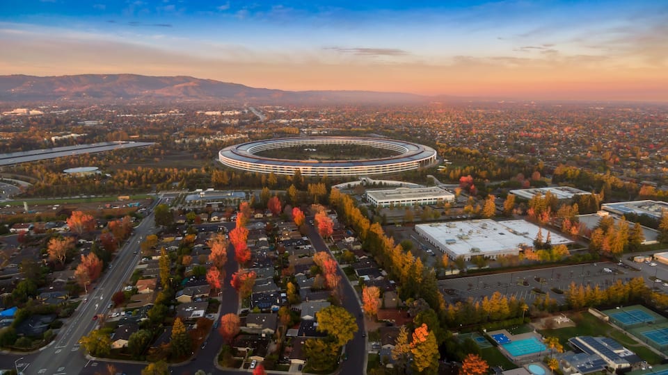 Vista aérea de uma paisagem urbana com um edifício circular marcante, áreas residenciais e folhagem outonal.