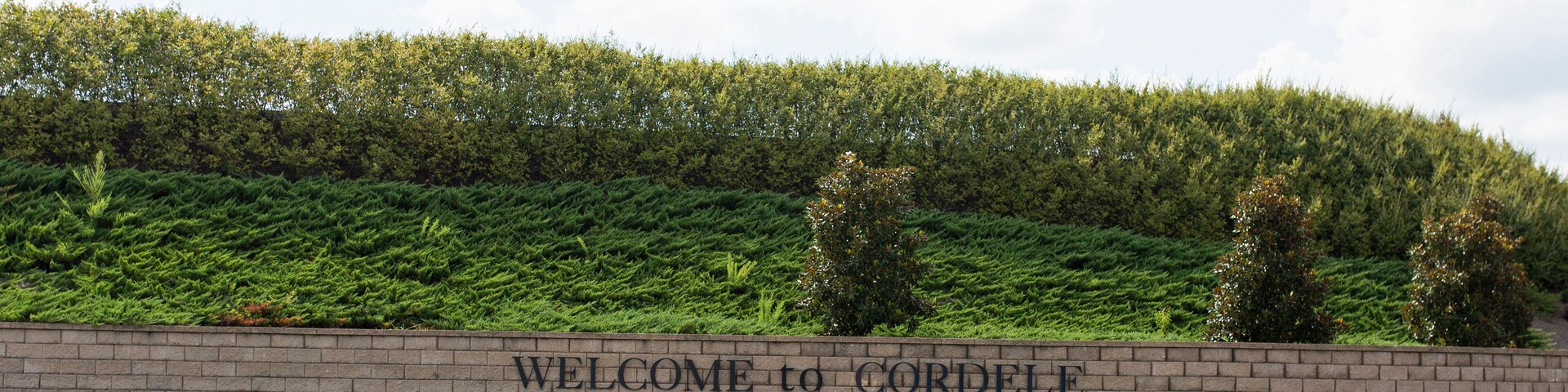 A brick wall with the inscription "WELCOME to Cordele" and a green lawn in the foreground.