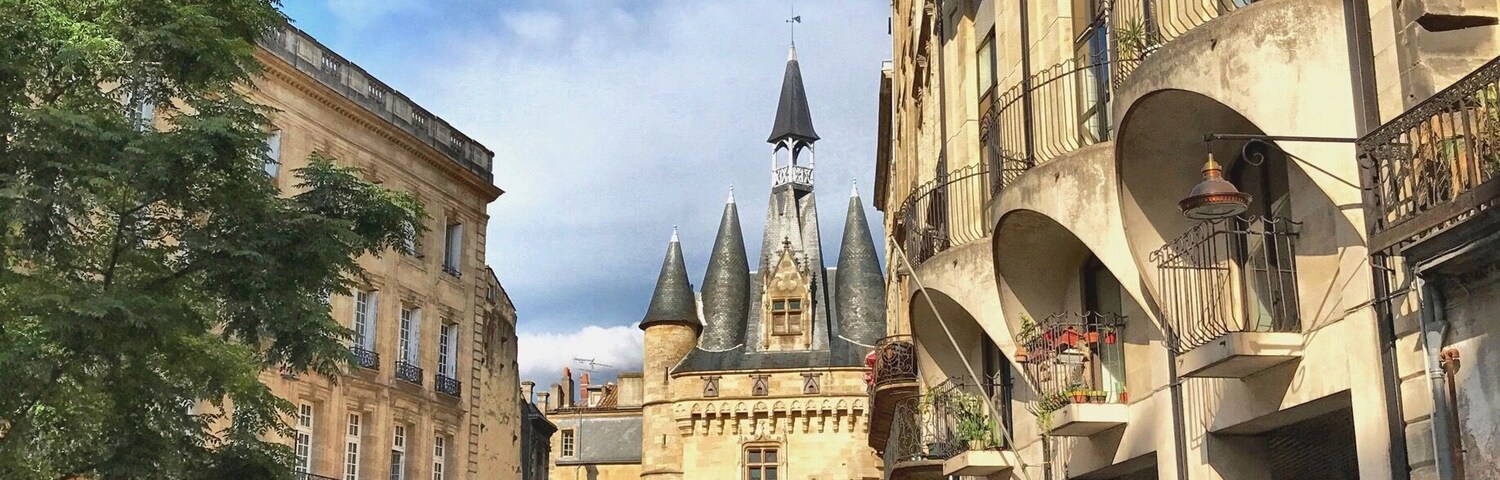 Uma rua de paraleipípedos flanqueada por edifícios históricos, uma torre imponente e um céu azul límpido.