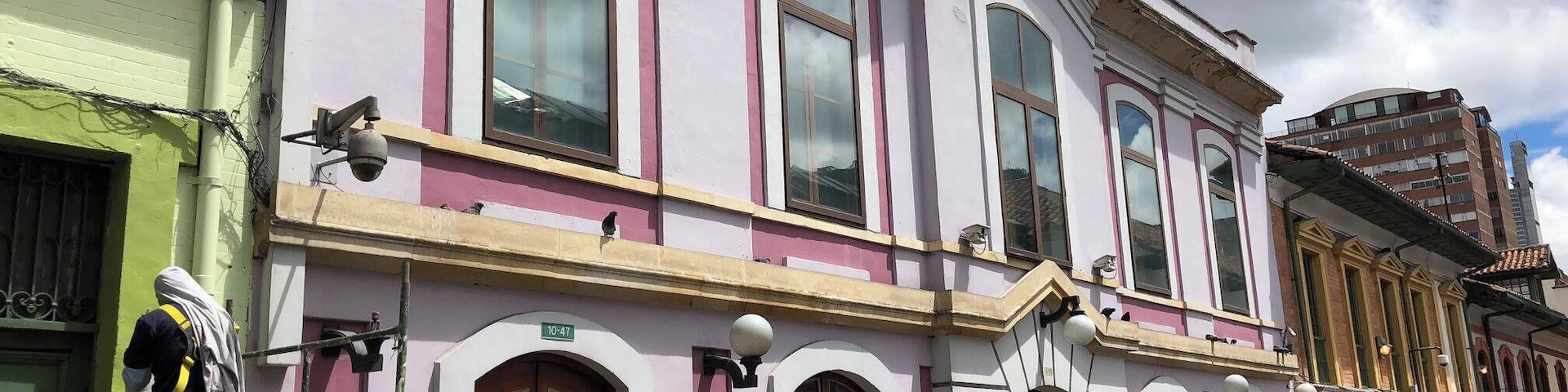 Um edifício histórico com fachada rosa e branca, janelas em arco e uma rua com uma pessoa em andaimes.