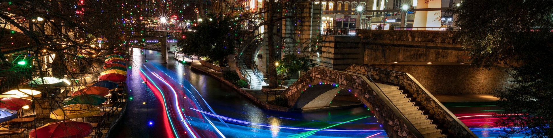 Paisagem urbana noturna com ruas iluminadas, uma ponte e uma grande escultura.