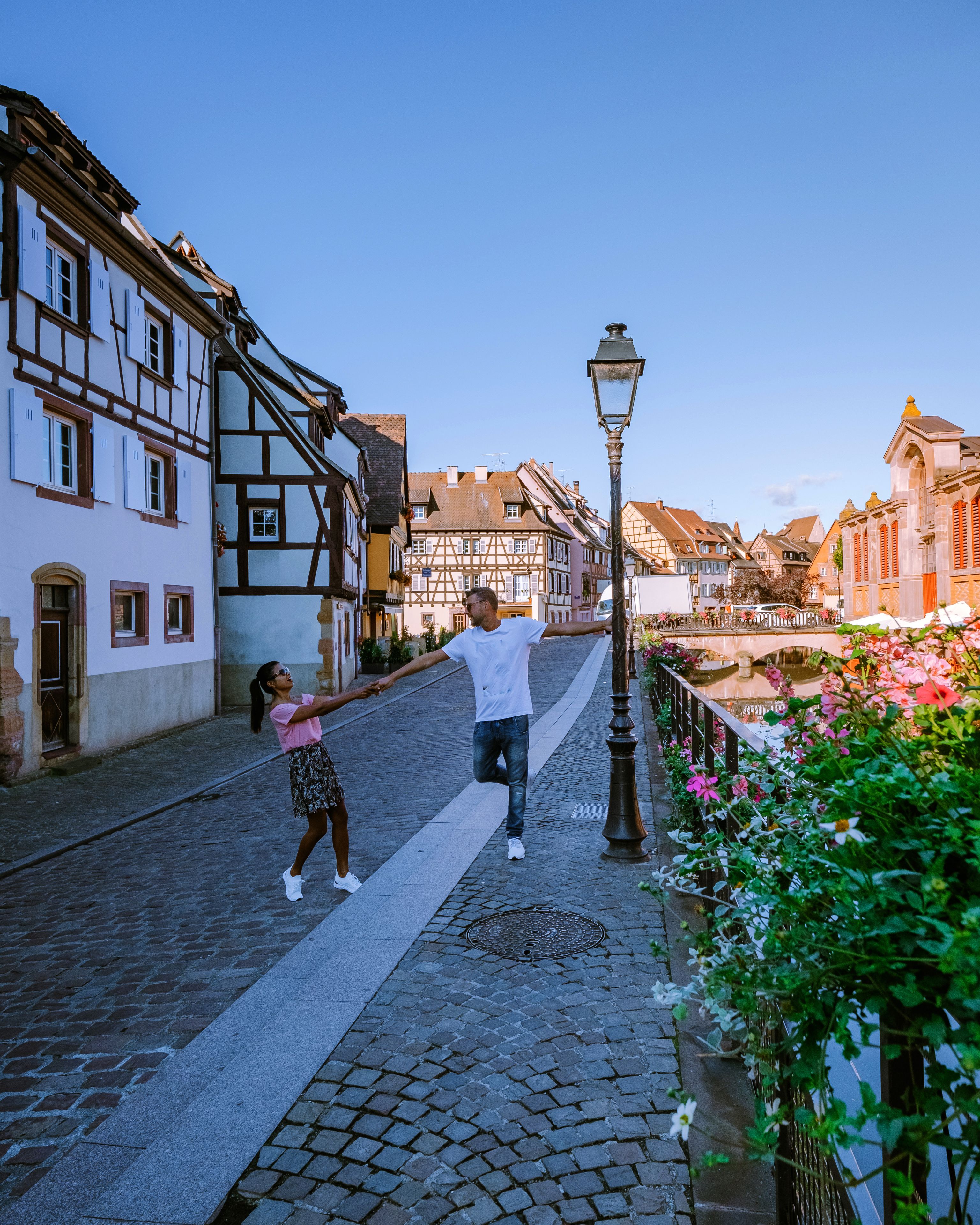 Ruas de paralelepípedos ladeadas por casas tradicionais de enxaimel, uma ponte e um canal com flores.