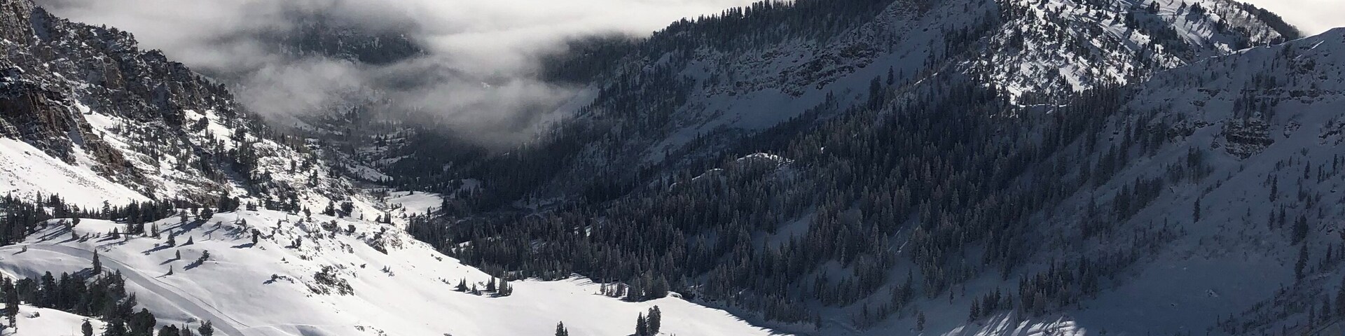 Paisagem nevada de montanhas, com um teleférico e um vale coberto de nuvens.