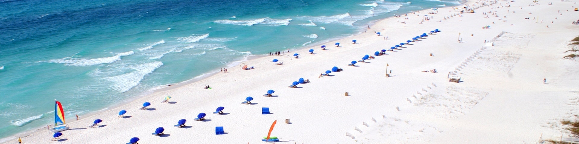 Uma praia com fileiras de guarda-sóis azuis e um píer que se estende para o oceano.