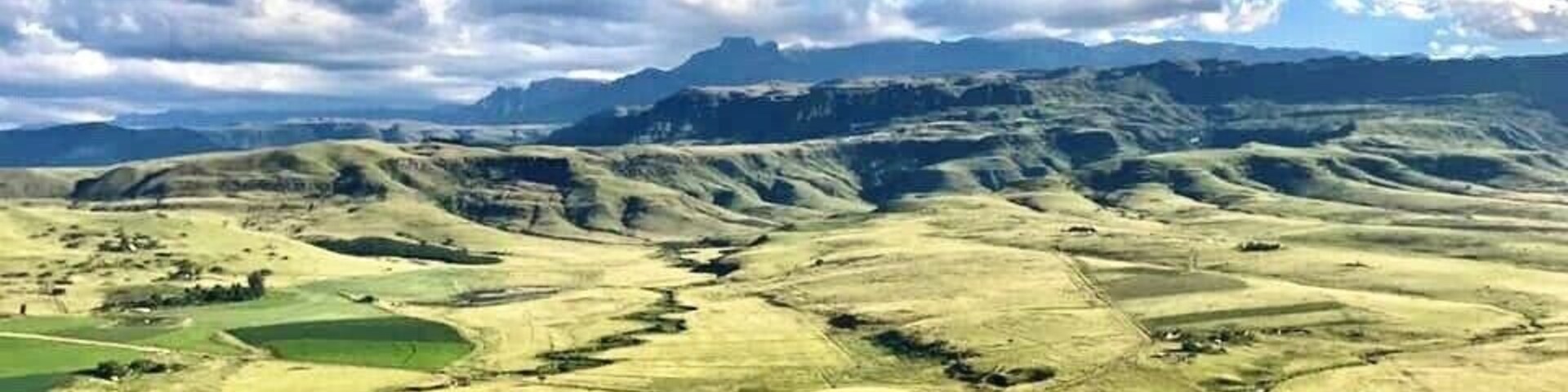 Colinas suaves, um rio e montanhas ao longe sob um céu parcialmente nublado.