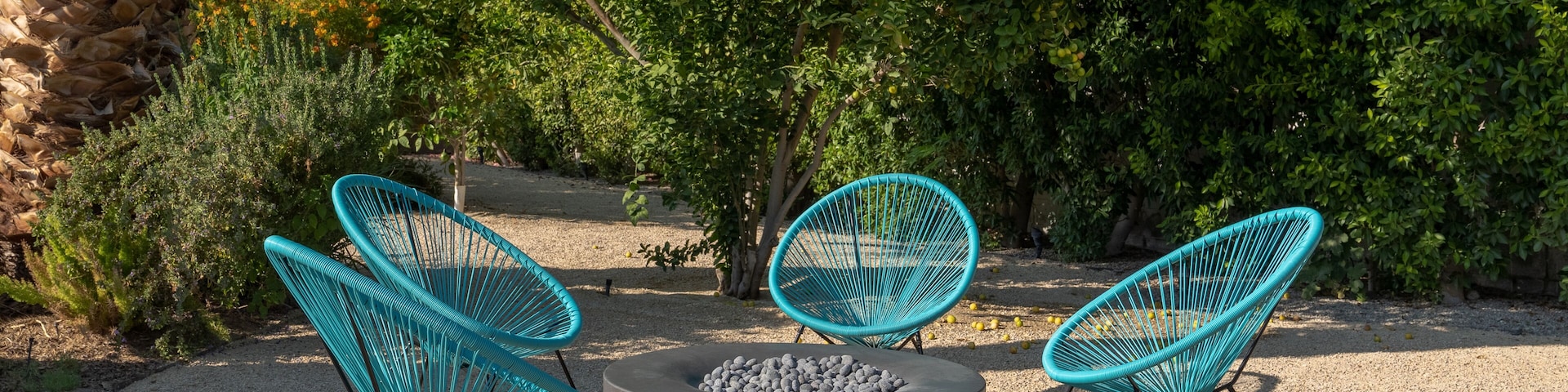 Uma lareira com três cadeiras turquesa num jardim.