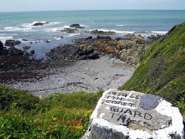 Litoral rochoso com uma placa que diz 'M39 45 Torre da Guarda Costeira'.